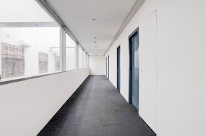 Um corredor longo e estreito com piso preto, paredes brancas e uma série de portas de um lado.
