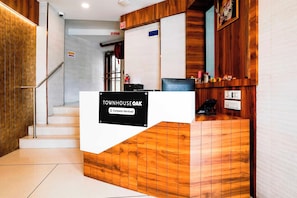 Uma mesa de recepção com uma placa indicando 'TOWNHOUSE OAK Company Serviced', um carretel de mangueira de incêndio e um monitor de computador Dell.