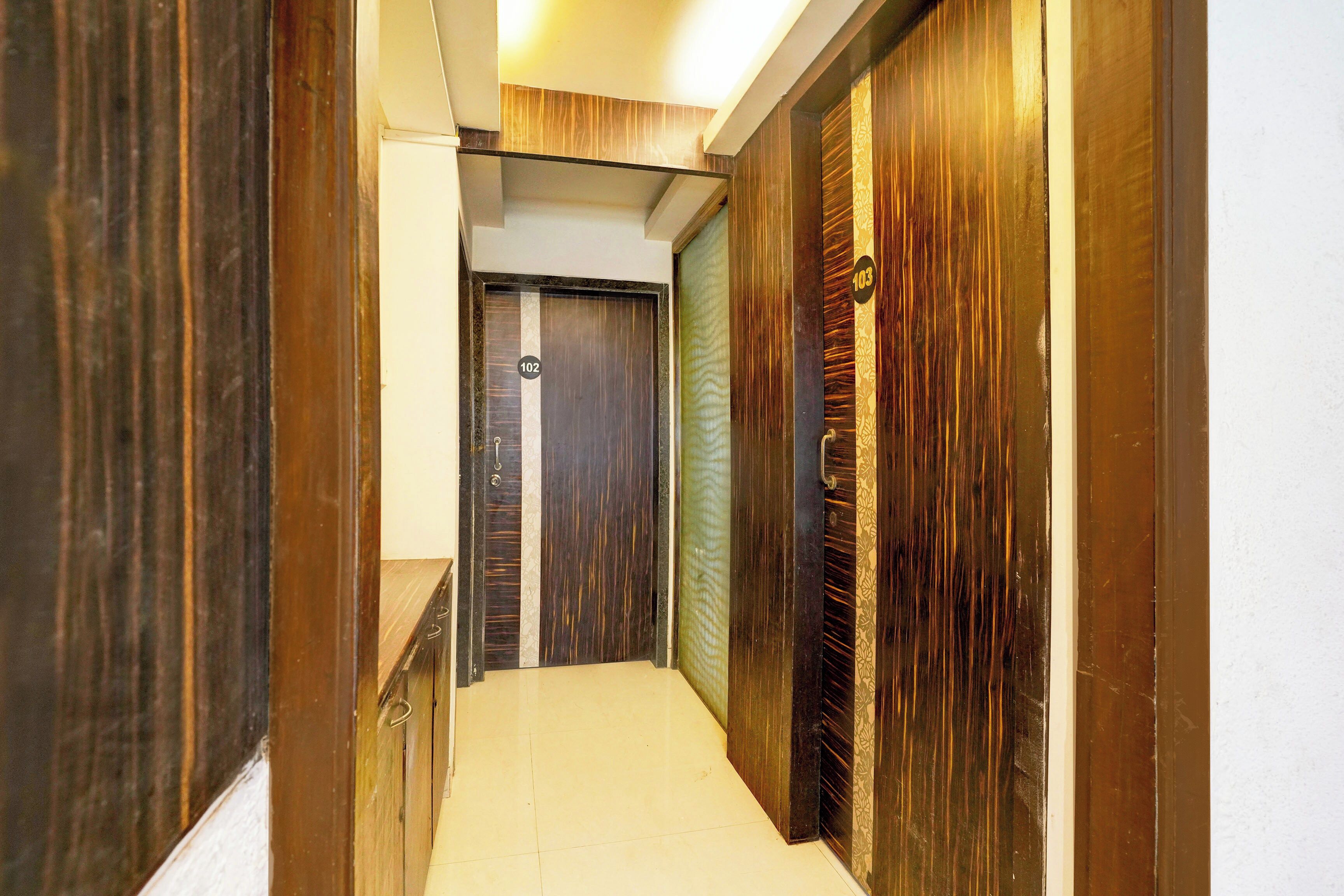 Corredor com portas de madeira, piso de azulejos e luminária no teto.