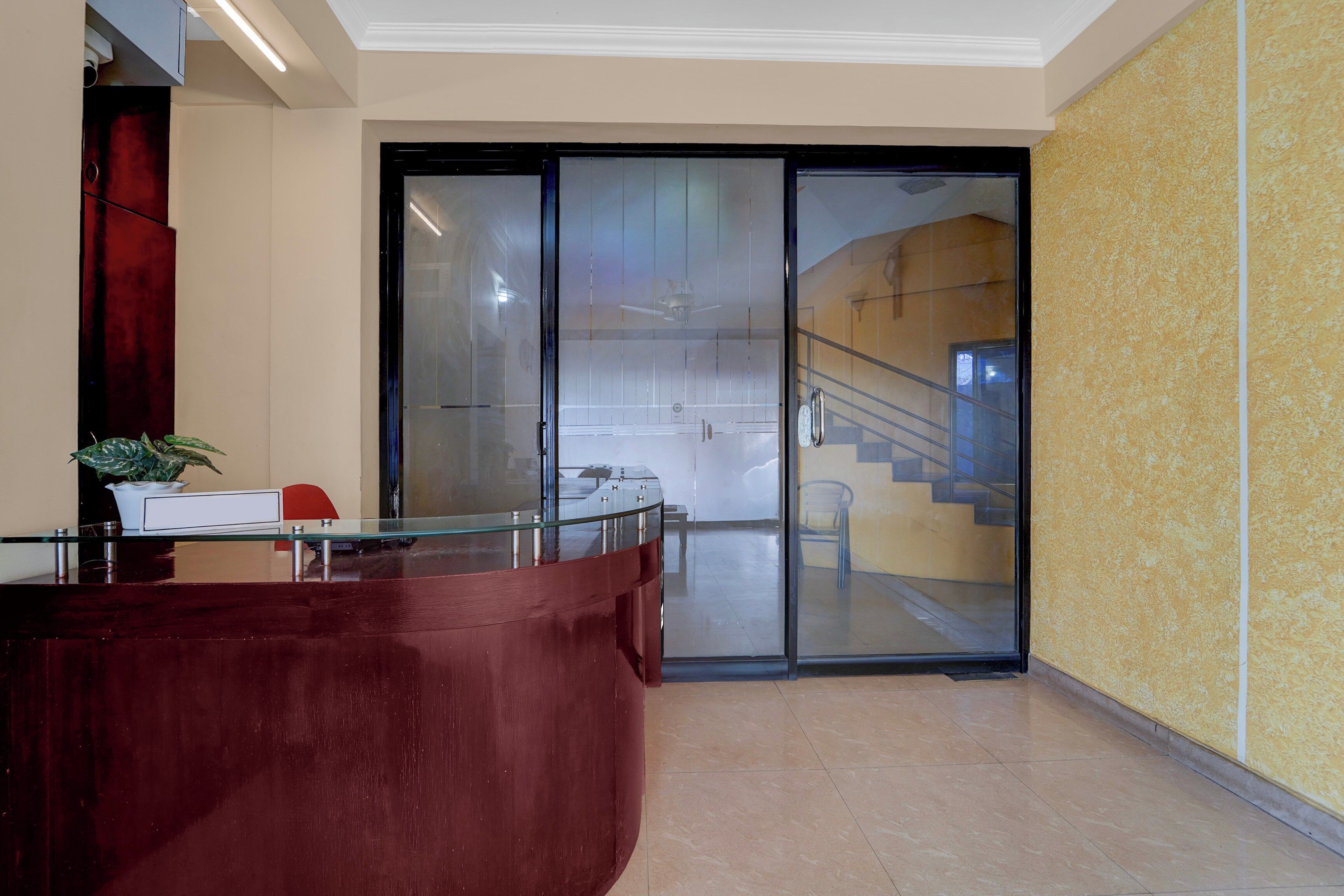 Uma área de recepção com divisória de vidro, balcão de atendimento, escada e parede amarela com textura.