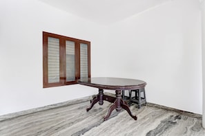 Quarto de canto com mesa redonda, armário de madeira e janela com painéis de vidro jateado.