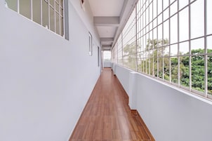 Um corredor comprido e estreito com piso de madeira e paredes brancas, que leva a uma área iluminada por janelas com vista para o verde.