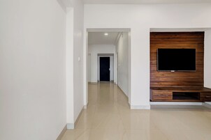 Corredor com televisão de tela plana fixada em um painel de madeira, que leva a um quarto escuro.