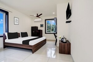 Quarto moderno com cama, ventilador de teto, janela com cortinas, televisão de tela plana e uma pequena mesa com chaleira.