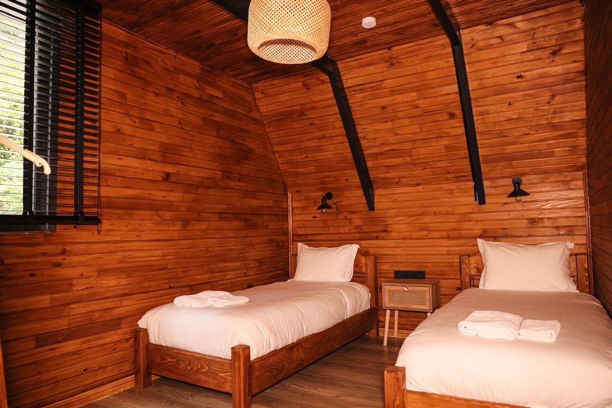 Quarto de cabana de madeira aconchegante, com duas camas, luminária pendente e janela com persianas.