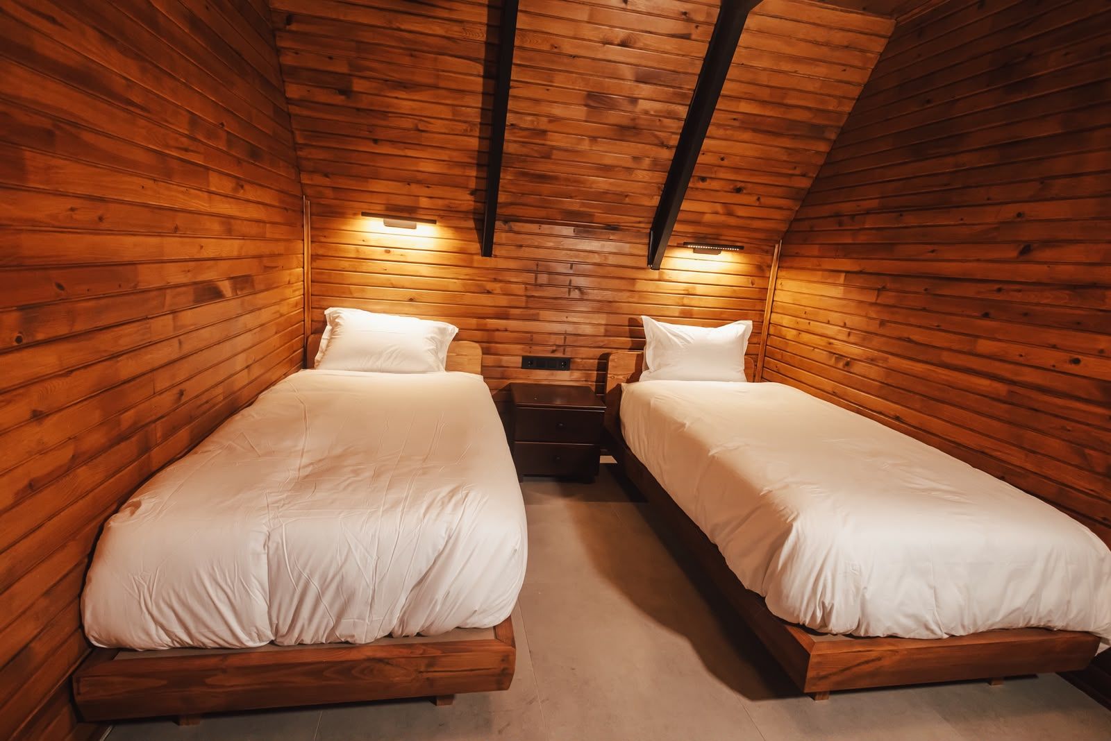 Uma cabana com duas camas de madeira, uma mesa pequena e um banco.