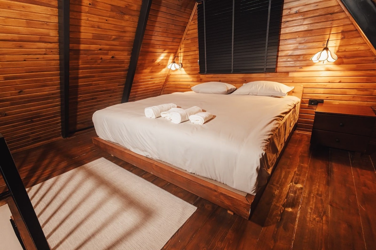 Quarto com painéis de madeira, uma cama, duas luminárias de cabeceira e uma mesinha de noite.