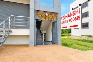 Entrada de um prédio com escadas que levam a uma porta, uma placa indicando 'VEDHANSHI LUXURY ROOMS' e um portão na entrada.