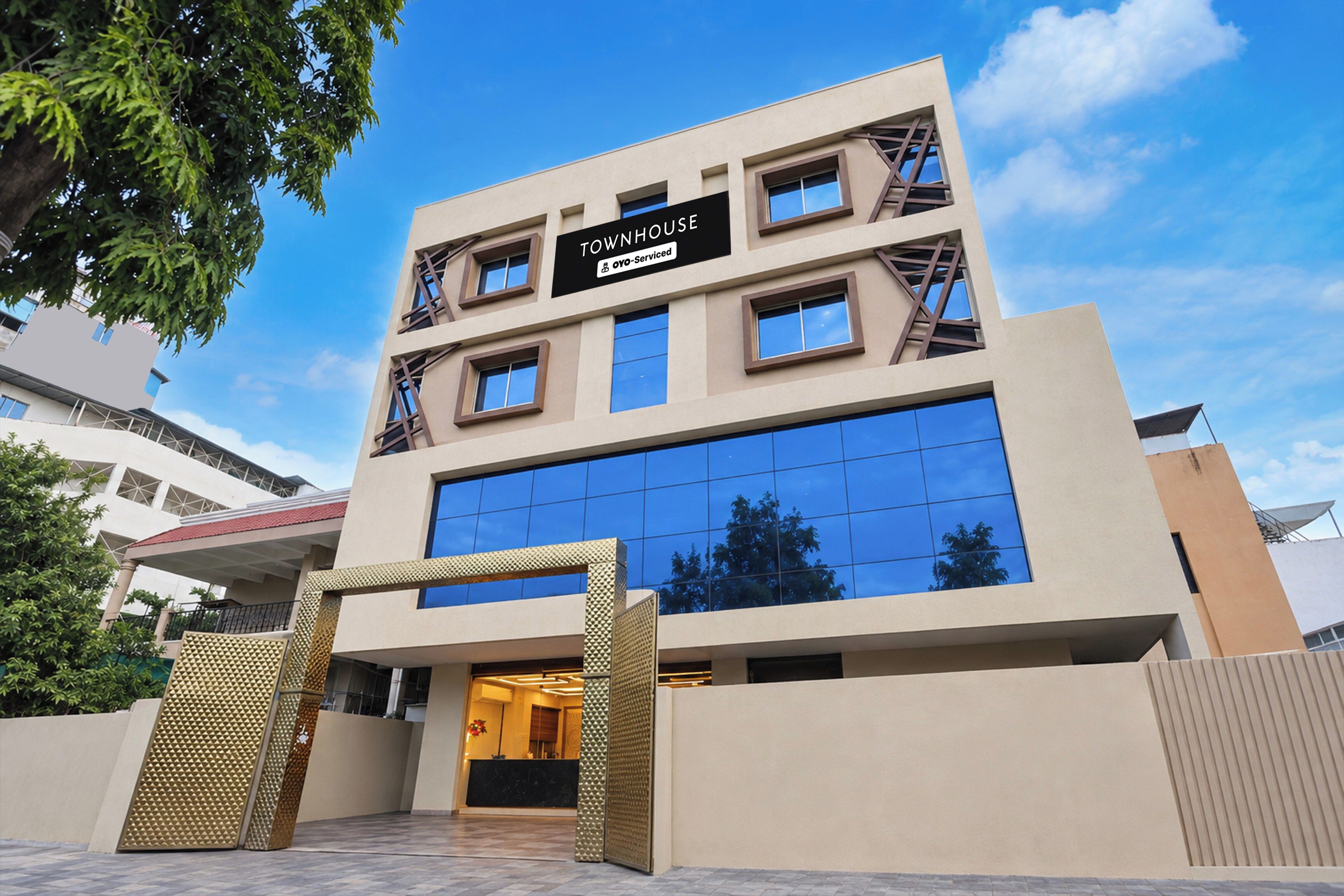Uma casa geminada moderna com fachada de vidro ampla, entrada destacada com design geométrico e placa indicando que é administrada pela OYO.