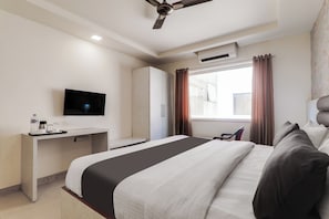 Quarto de hotel com cama, escrivaninha, televisão de tela plana, guarda-roupa e ar condicionado.
