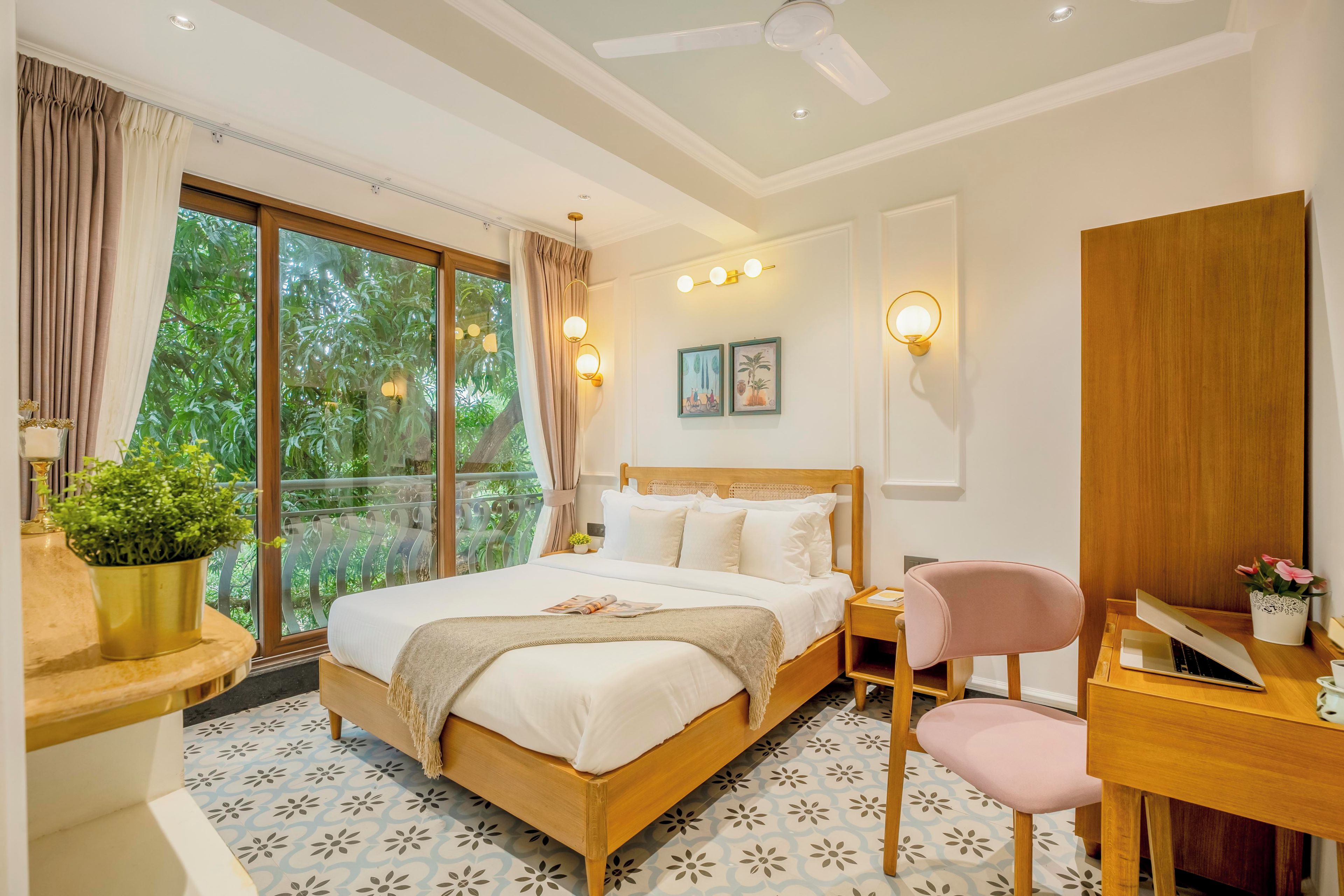Quarto de hotel com uma cama grande, uma escrivaninha com cadeira, um laptop e um vaso de planta.