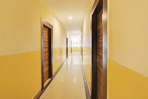 Corredor comprido e estreito com portas em ambos os lados, que dá para um quarto iluminado ao fundo.