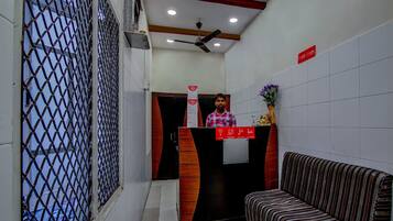Uma área de recepção com balcão, sala de espera com sofá listrado e ventilador de teto.