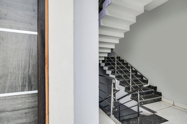Uma escadaria moderna com corrimão de metal e degraus pretos, que leva a um patamar com parede branca.