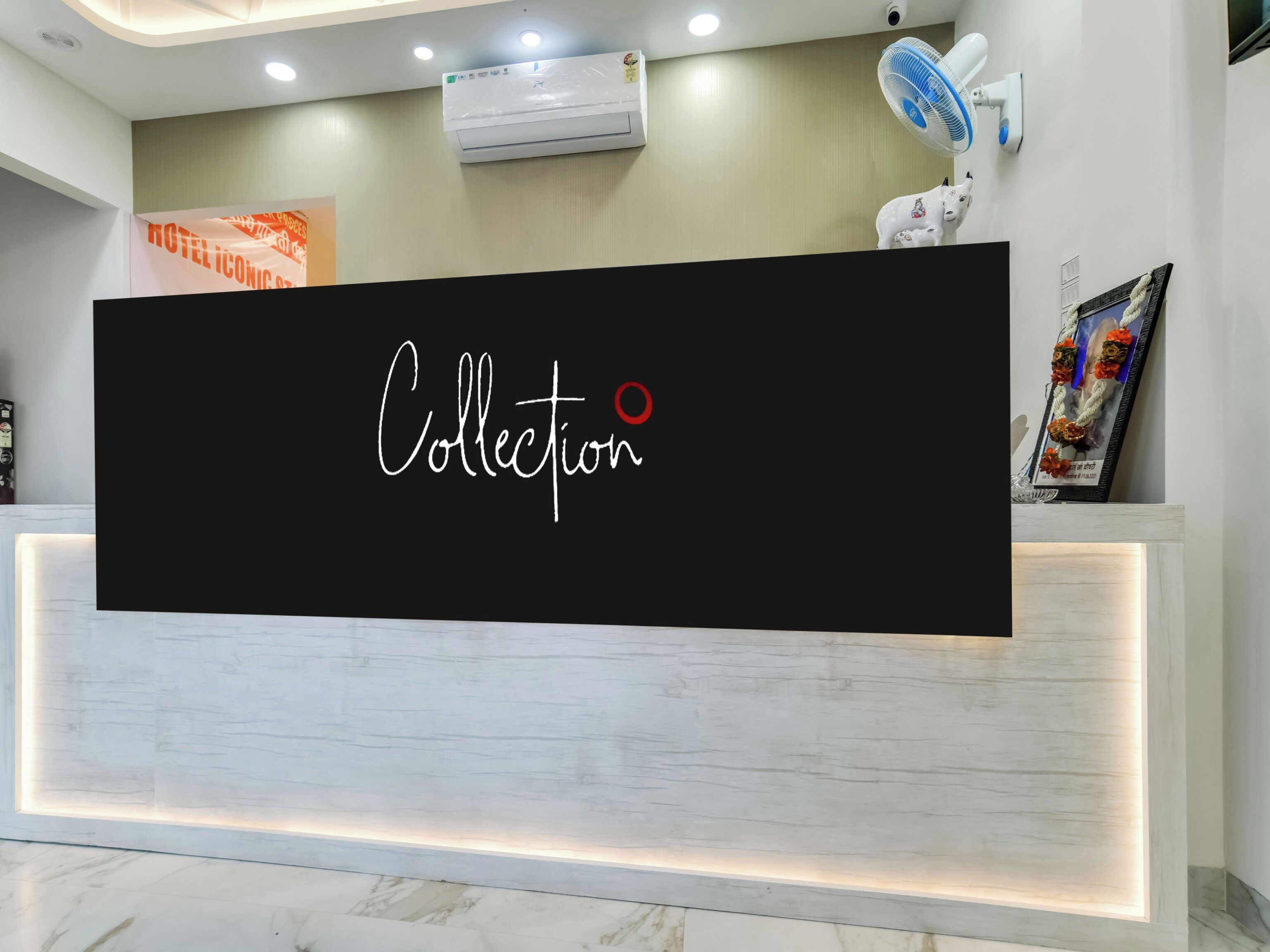 Balcão de recepção com uma grande placa preta com a palavra 'Collection' e uma parede branca com um quadro emoldurado.