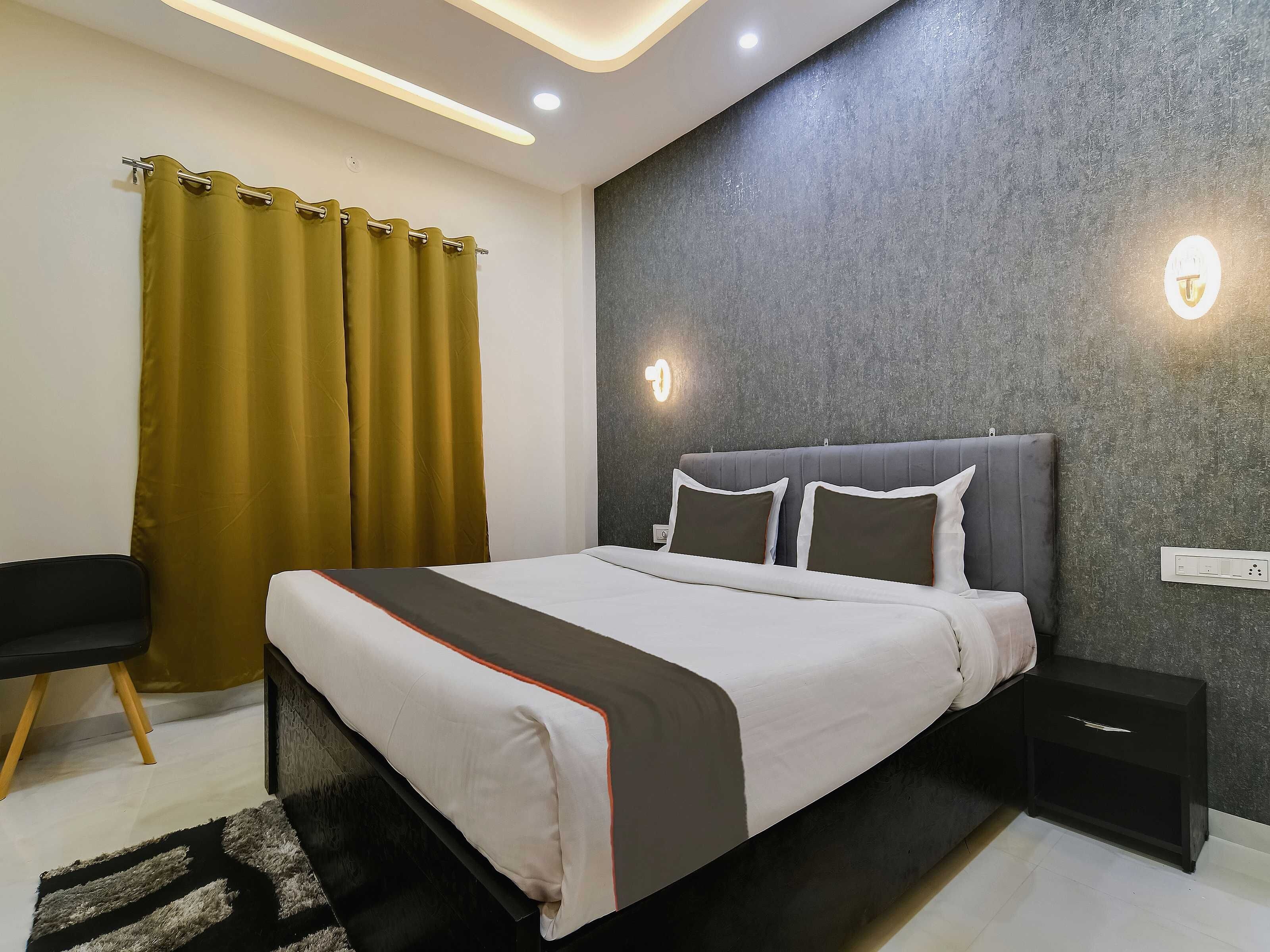 Quarto de hotel moderno com cama, mesas de cabeceira, uma cadeira e cortina.