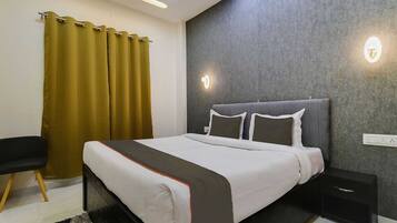 Quarto de hotel moderno com cama, mesas de cabeceira, uma cadeira e cortina.