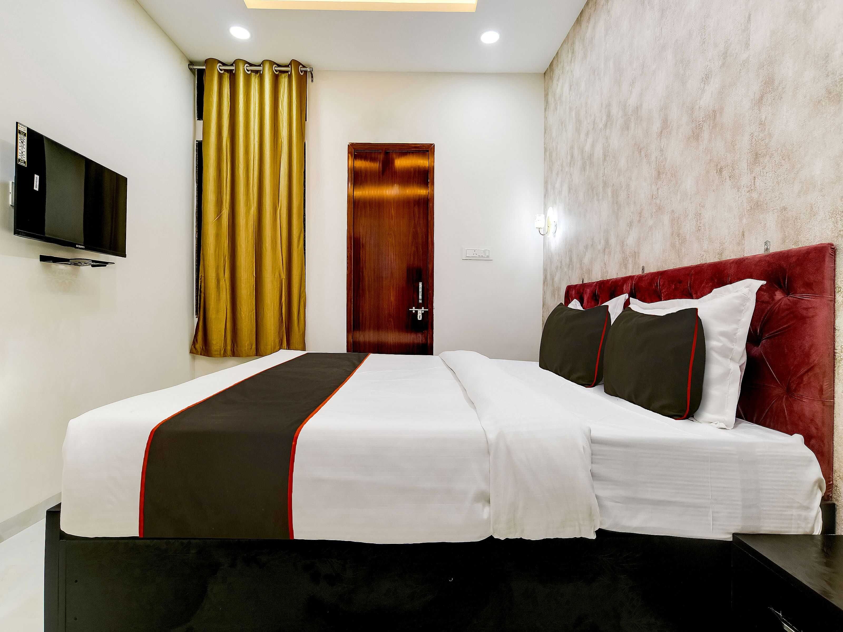 Quarto de hotel com uma cama, televisão, porta e cortina.