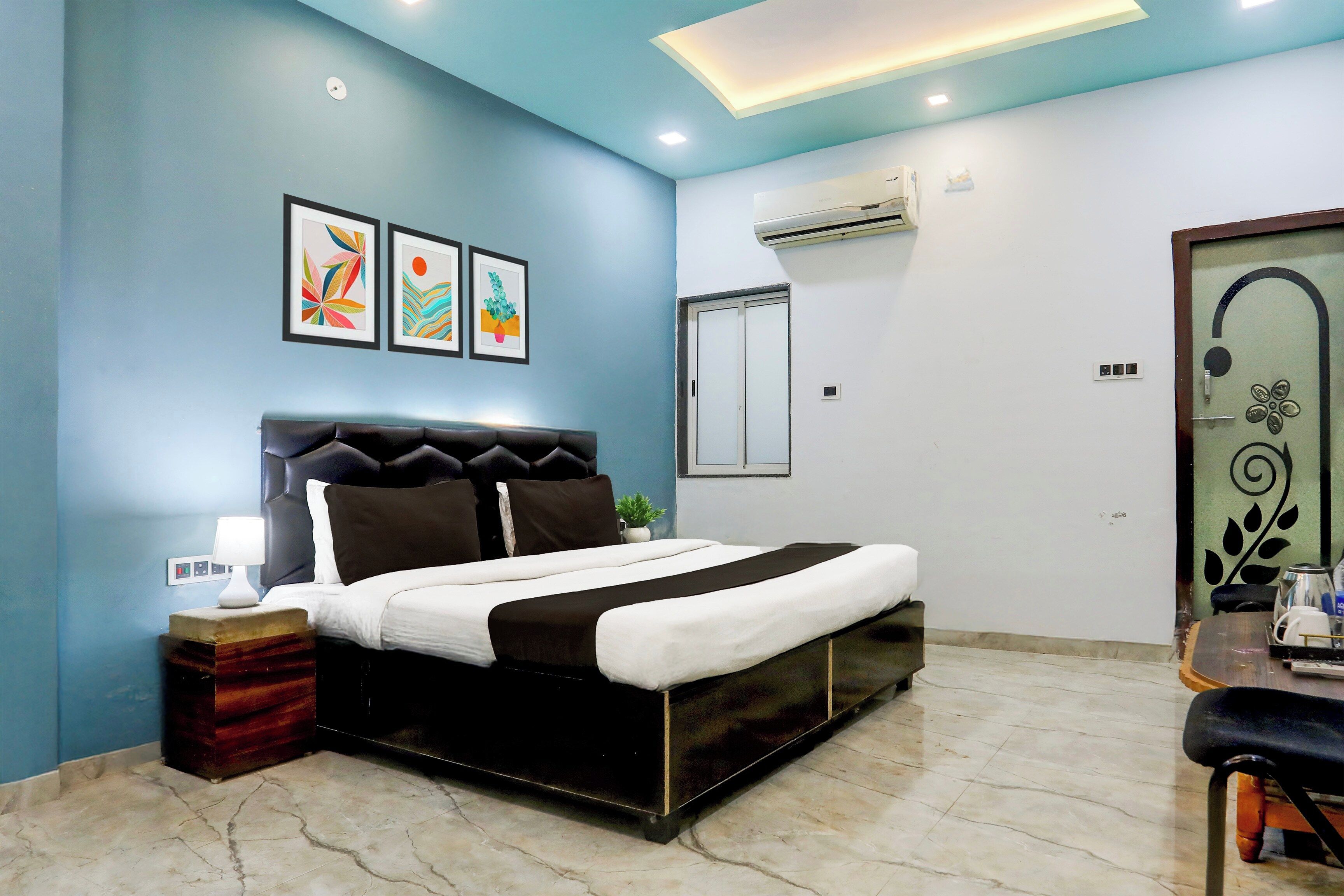 Quarto com cama, mesa de cabeceira, ar condicionado fixado na parede e porta com detalhes decorativos.