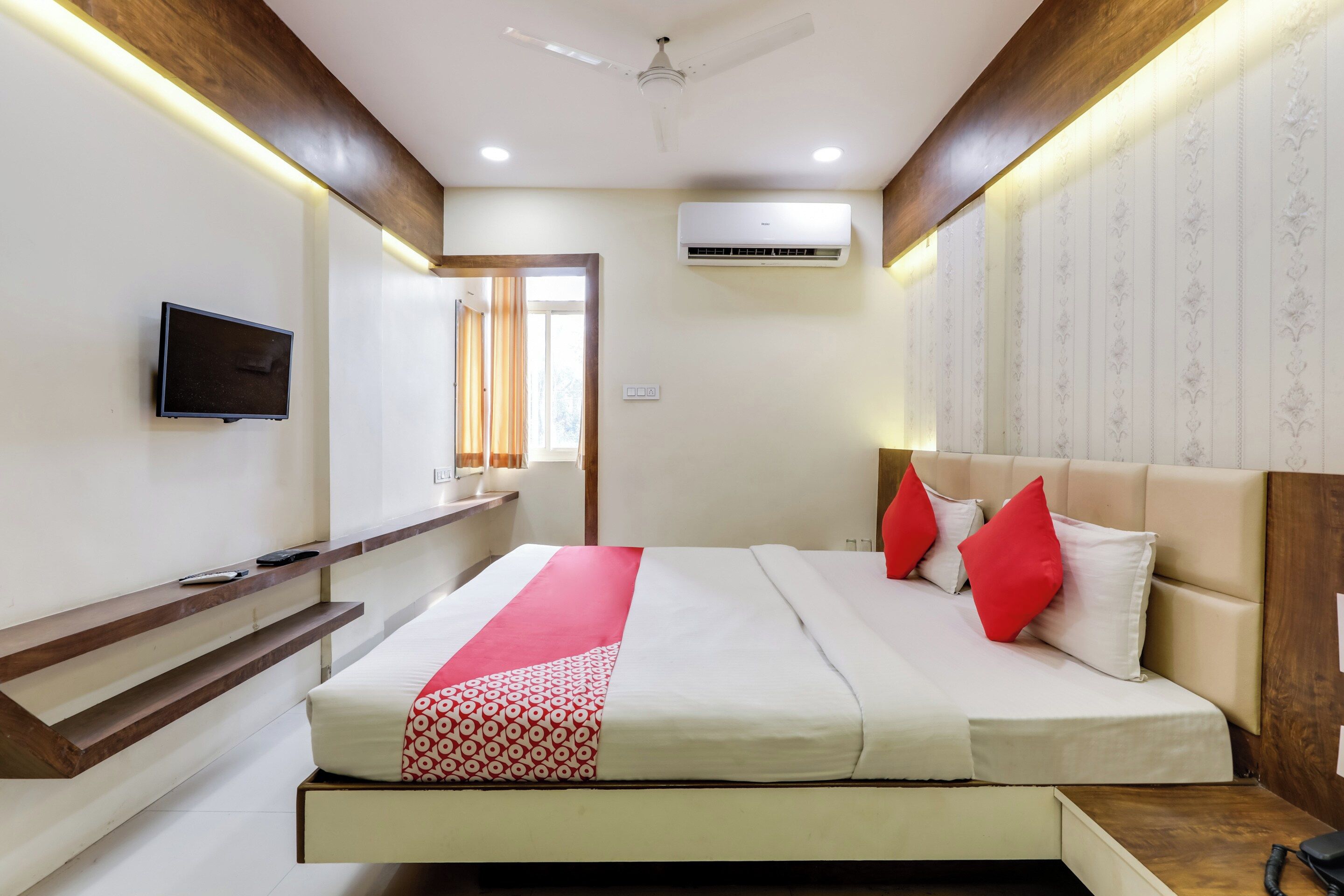 Quarto de hotel com cama, televisão, ar condicionado e janela com cortinas.