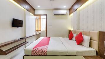 Quarto de hotel com cama, televisão, ar condicionado e janela com cortinas.