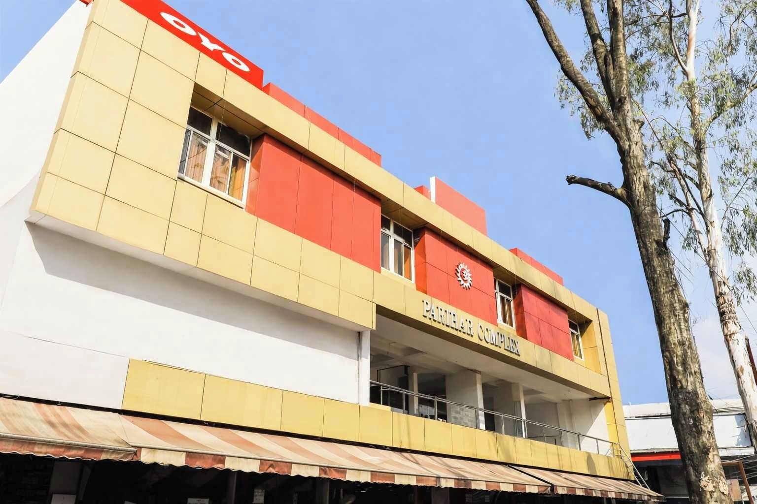 Um edifício de vários andares com uma fachada marcante em vermelho e amarelo, um letreiro com a inscrição 'PARALLEL COMPLEX' e uma varanda visível no andar térreo.