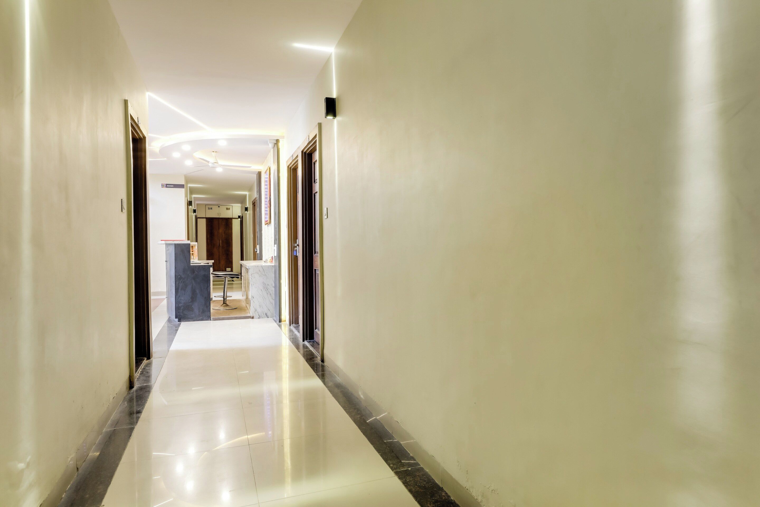 Corredor de hotel com piso de mármore, portas em ambos os lados e uma mesa de recepção ao fundo.