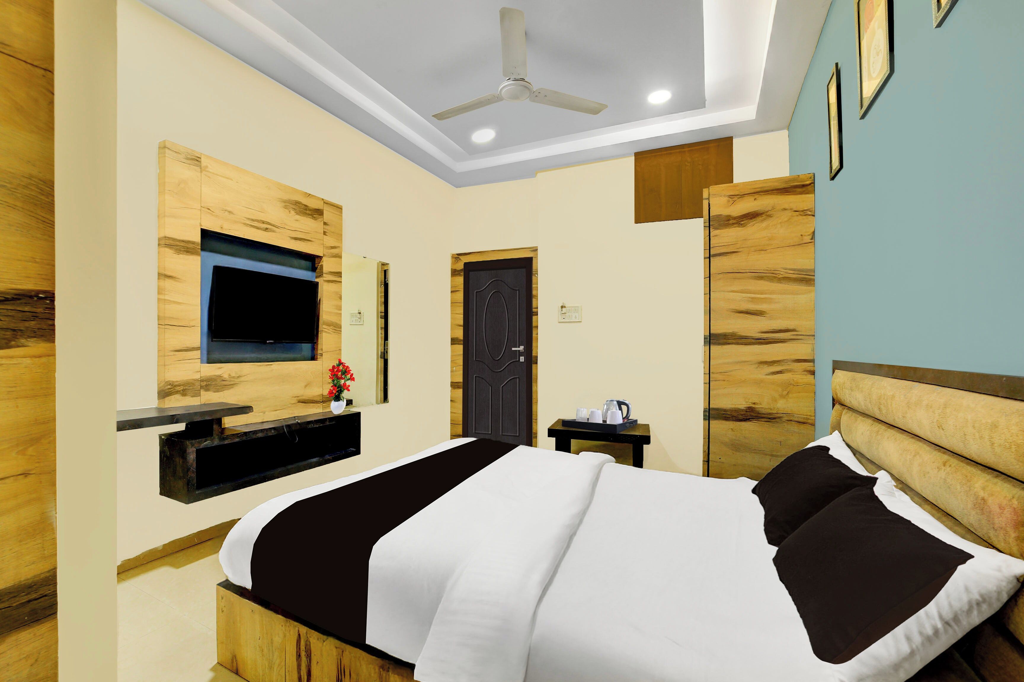 Quarto de hotel com cama, televisão na parede, mesinha com bandeja e ventoinha no teto.