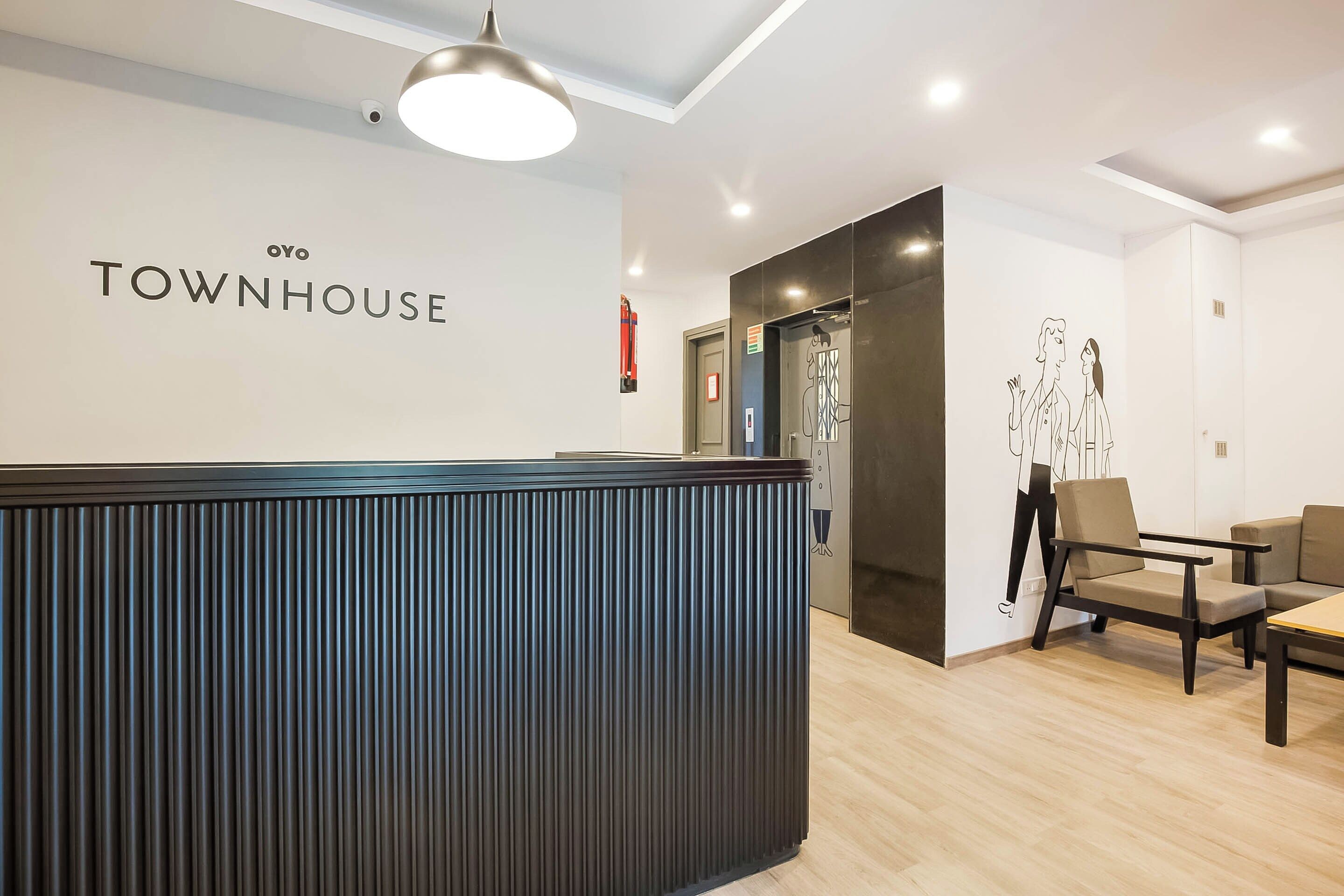 Uma mesa de recepção com design moderno, um letreiro com a palavra 'TOWNHOUSE' e uma área de estar com duas cadeiras.