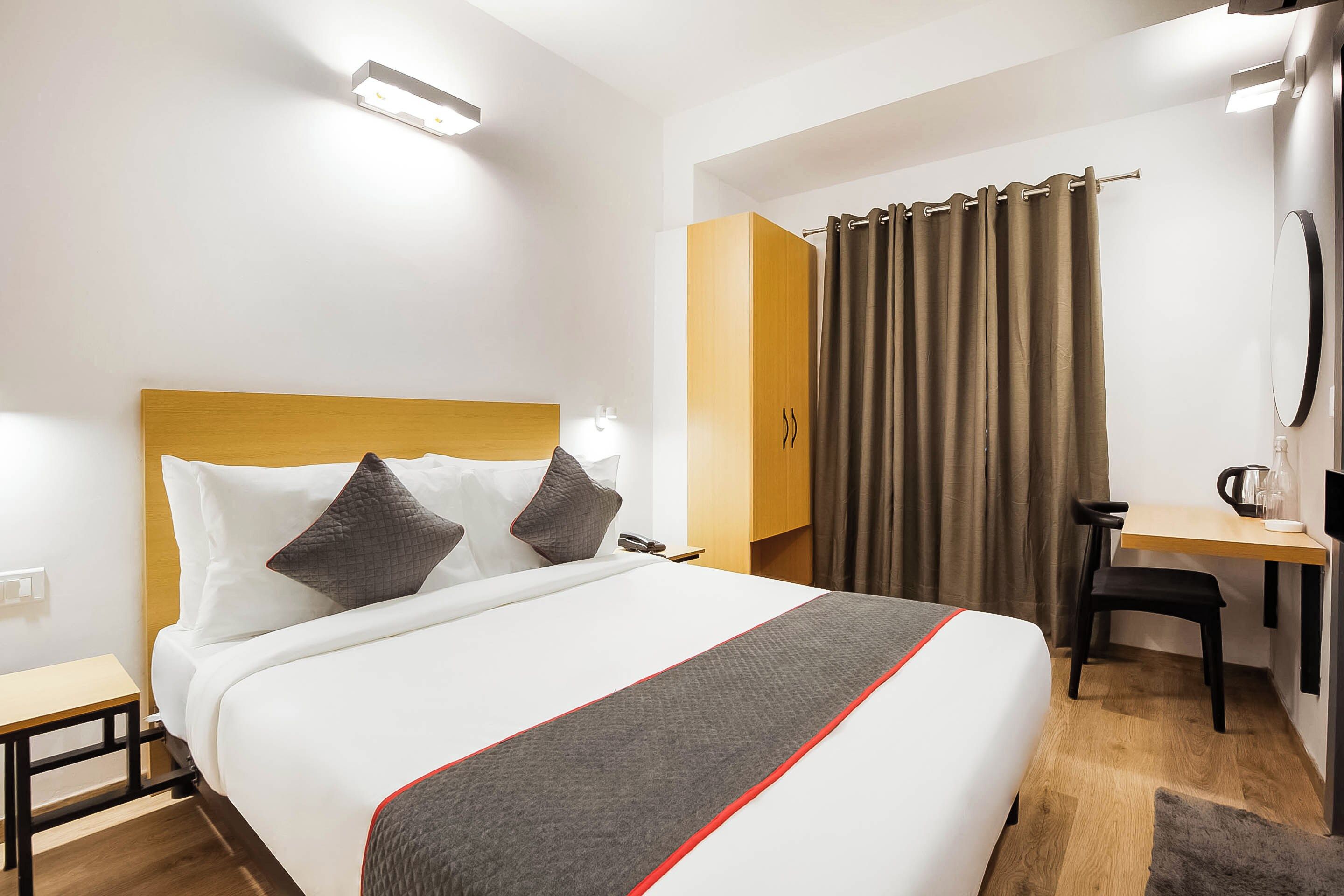 Quarto de hotel com cama, mesa de cabeceira, escrivaninha, cadeira e guarda-roupa.