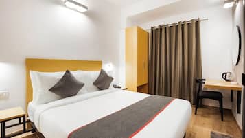 Quarto de hotel com cama, mesa de cabeceira, escrivaninha, cadeira e guarda-roupa.