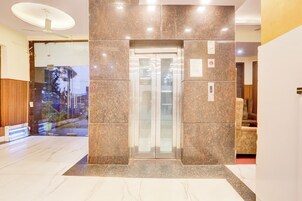Elevador moderno com porta de vidro, em meio a paredes de granito, em um hall bem iluminado.