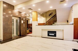 Um saguão de hotel com balcão de recepção, escada e elevador de vidro.