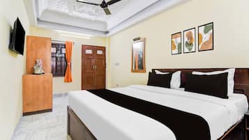 Quarto de hotel com uma cama, ventoinha no teto, televisão, guarda-roupa e uma porta com janela.