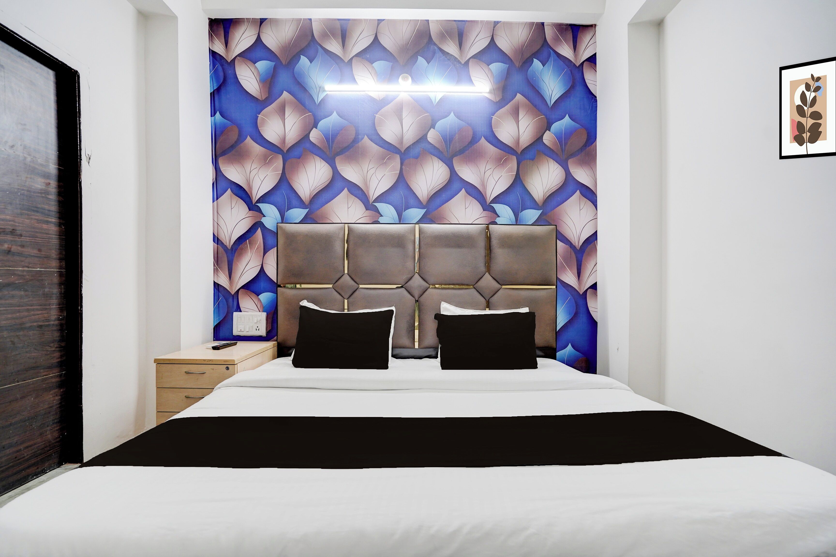 Quarto com cama, duas almofadas, mesa de cabeceira, luminária na parede e papel de parede estampado.