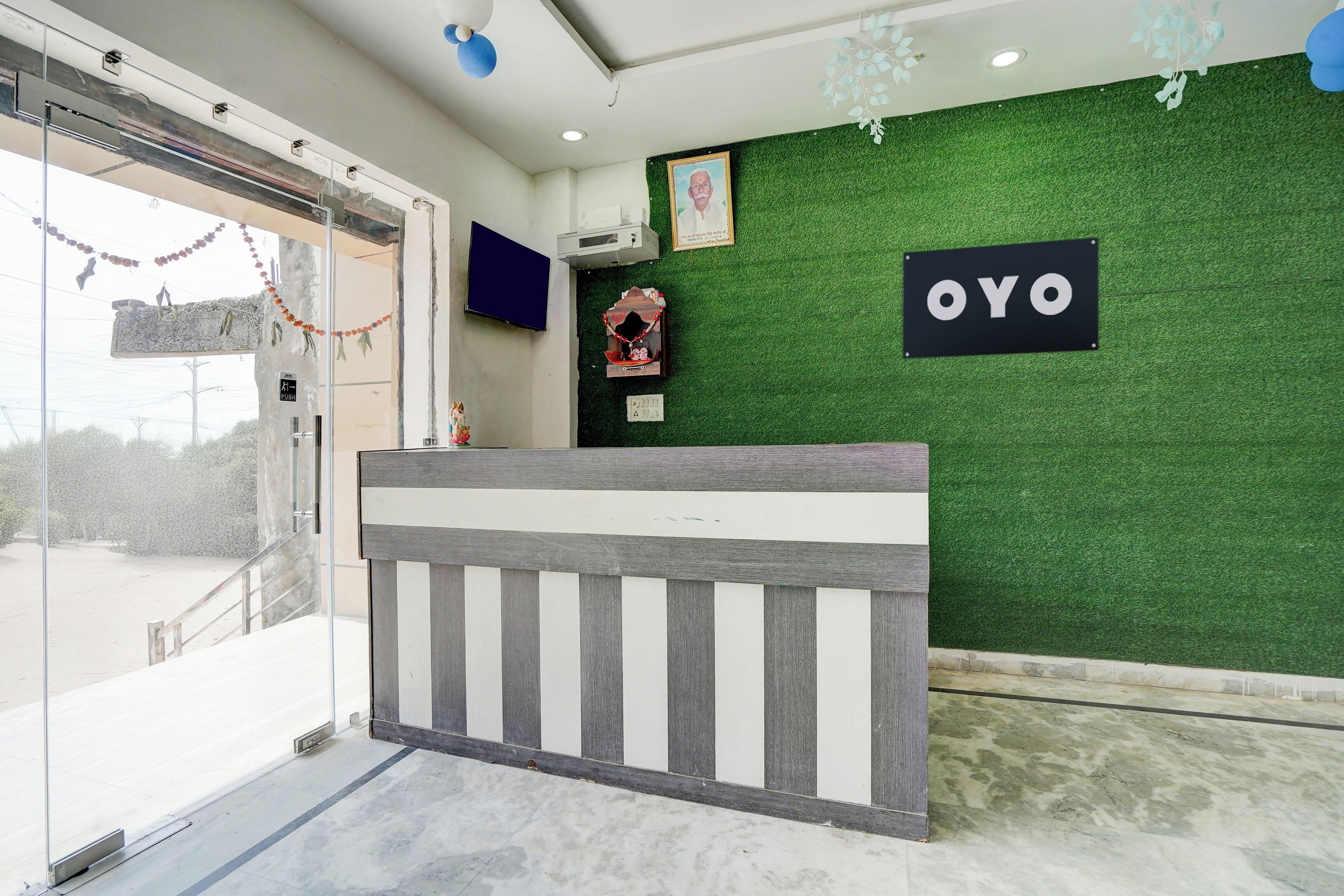 Uma área de recepção com parede verde, uma placa com a inscrição 'OYO' e um pequeno santuário.