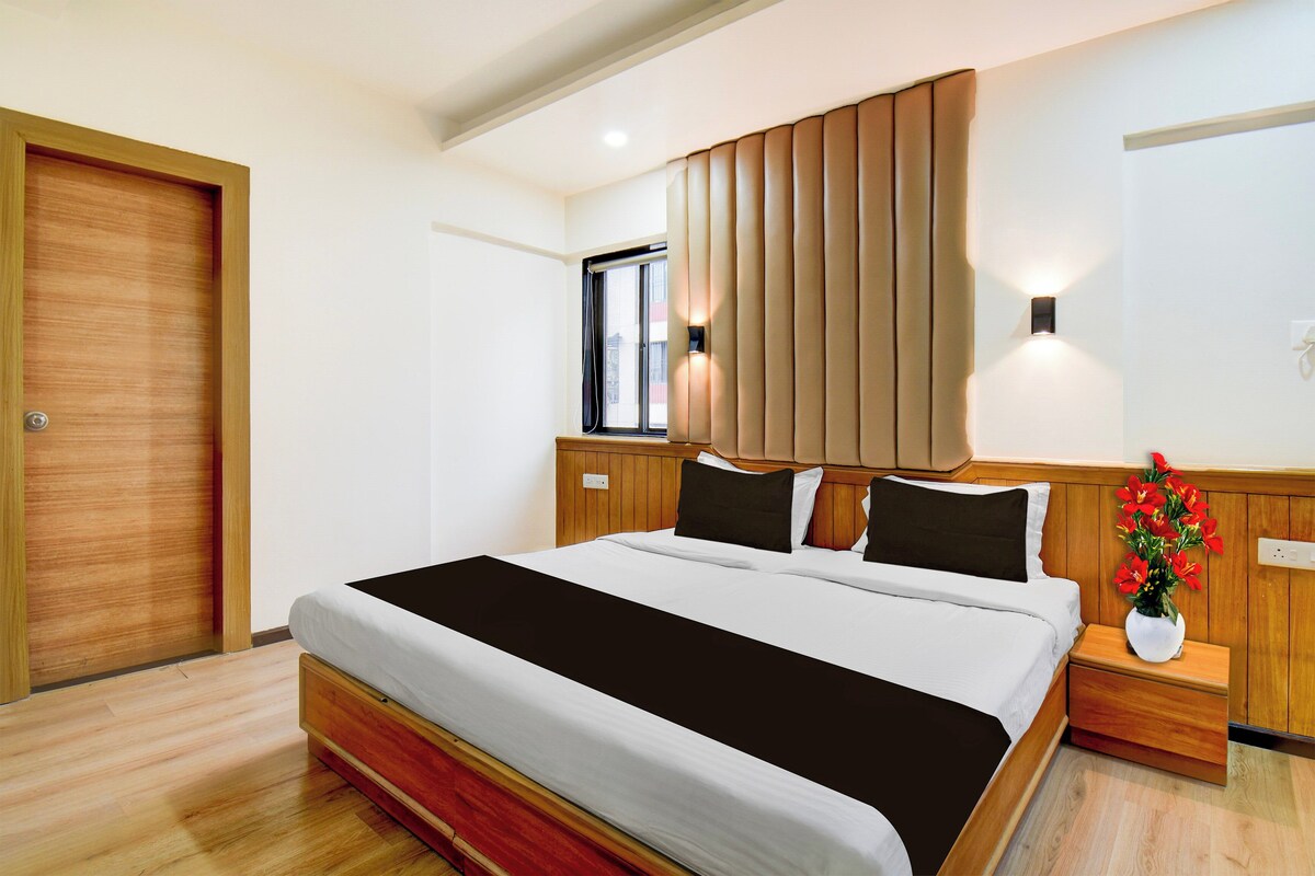 Quarto de hotel moderno com uma cama grande, cabeceira de madeira, mesa de cabeceira, luminária na parede e janela com cortinas.