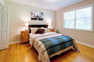 Quarto com cama, duas mesas de cabeceira, um criado-mudo, janela com persianas e um quadro na parede.