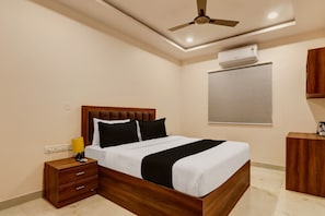 Quarto de hotel com cama, mesa de cabeceira, luminária, ventilador de teto, aparelho de ar condicionado e janela.