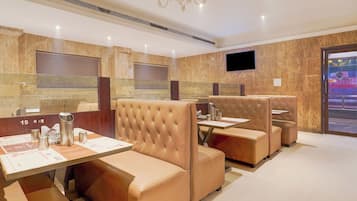 Restaurante de hotel com assentos em cabines, televisão de tela plana e um lustre moderno.