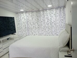 Quarto com cama, televisão, mesa de cabeceira e cortina com padrão de pena.