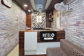 Uma receção de hotel com balcão de madeira, uma placa com a inscrição 'HOTEL OYO-Serviced' e uma parede estampada ao fundo.