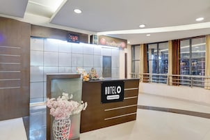 Balcão de recepção de hotel com placa 'HOTEL', relógio e um vaso decorativo com flores.