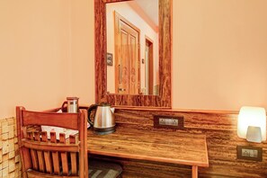 Espelho com moldura de madeira refletindo uma porta, uma chaleira e uma bandeja com uma cafeteira sobre uma mesa de madeira.