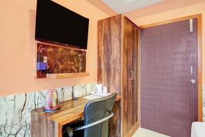 Quarto com escrivaninha de madeira, cadeira, televisão na parede e guarda-roupa com espelho.