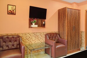Quarto com duas poltronas de couro, uma mesa de vidro, um armário de madeira, uma televisão e um quadro pendurado na parede.