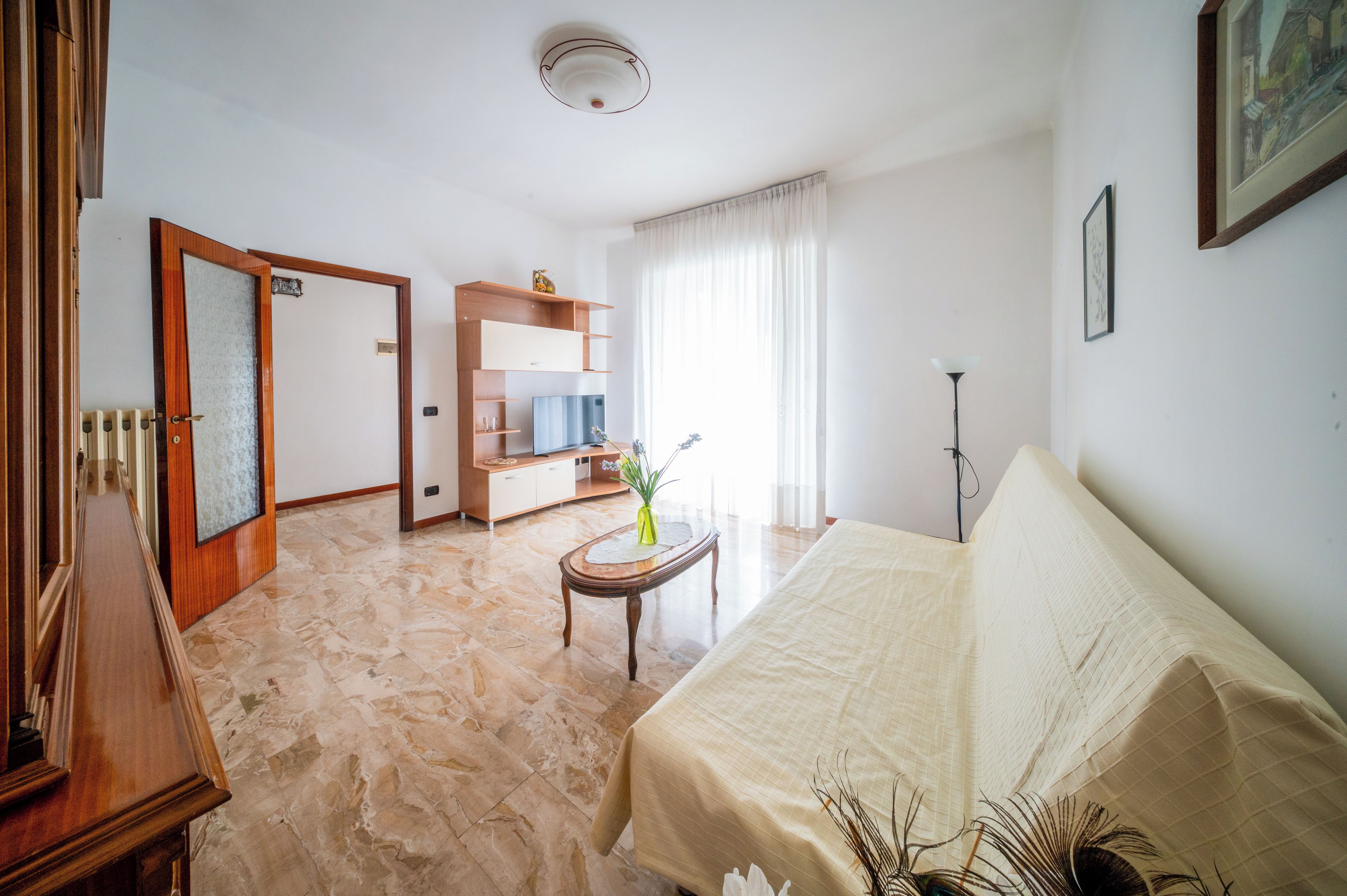 Quarto de hotel com cama, televisão, mesinha com um vaso, armário de madeira e uma porta.