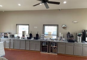 Cozinha moderna com armários cinza, micro-ondas embutido, máquinas de café e geladeira.