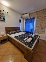 Quarto com cama, mesa de cabeceira, luminária, ar-condicionado fixado na parede e janela com cortina.