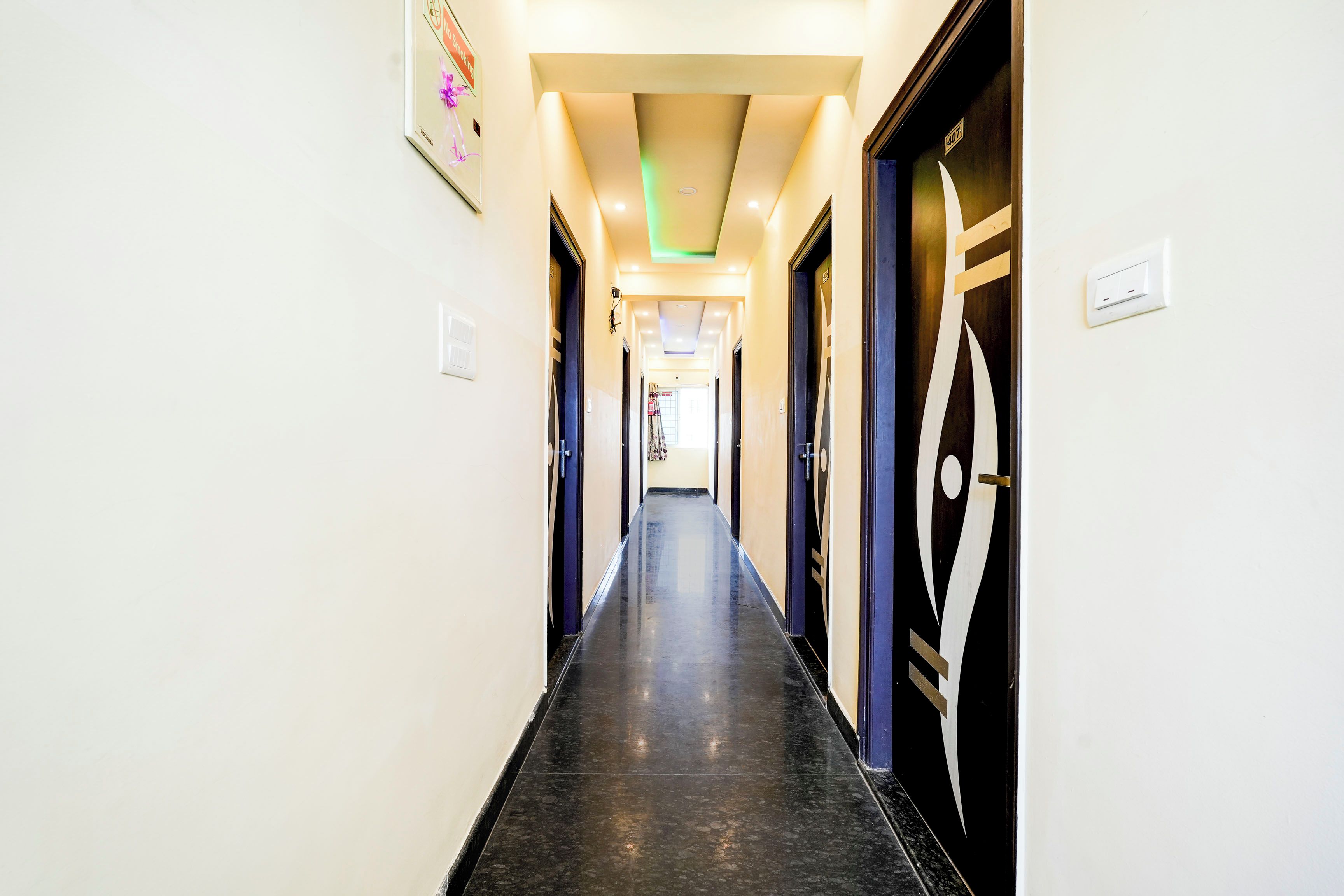 Corredor de hotel com portas em ambos os lados, piso em tons claros e teto com iluminação embutida.
